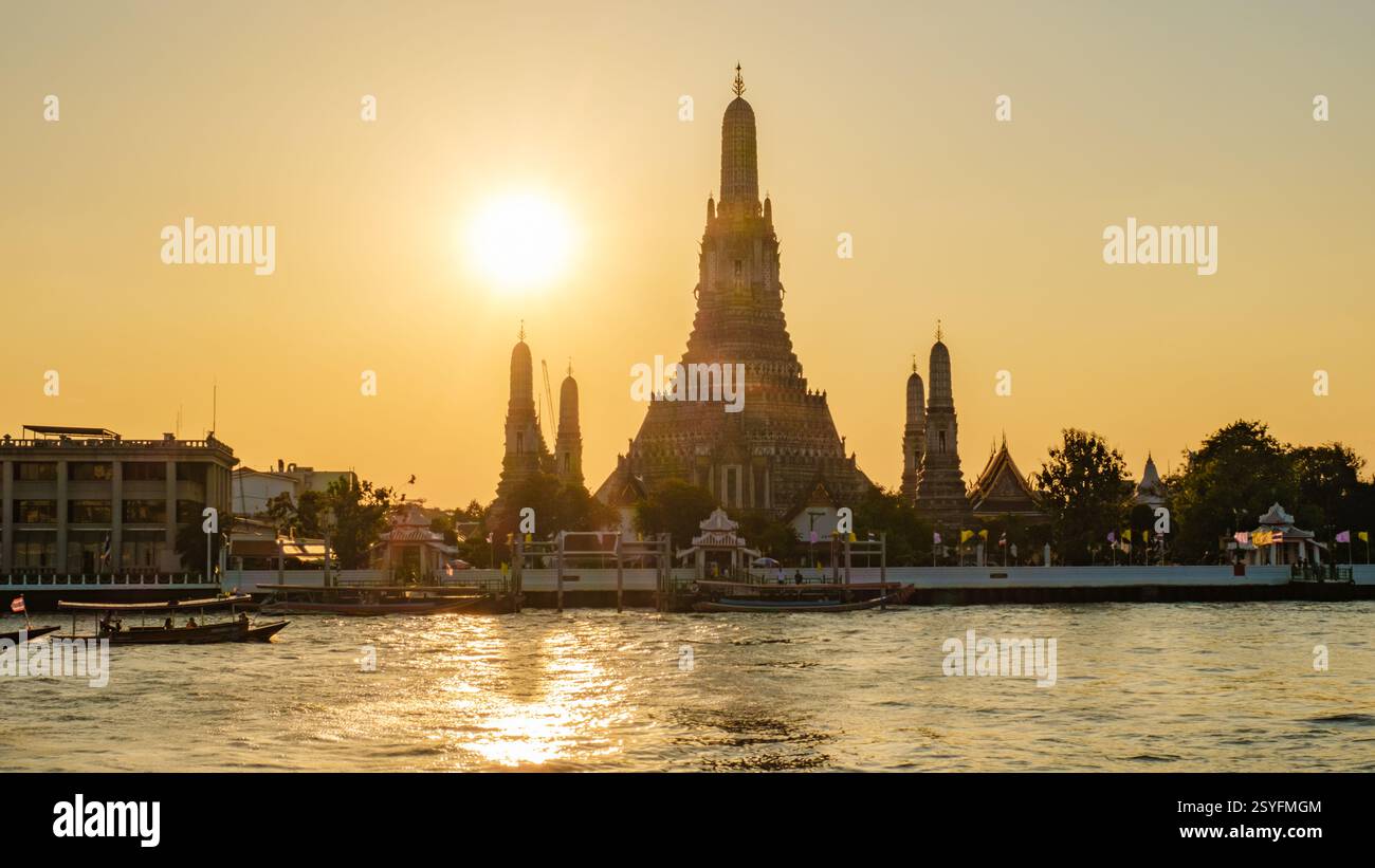As the sun sets behind the majestic Wat Arun temple, its intricate ...