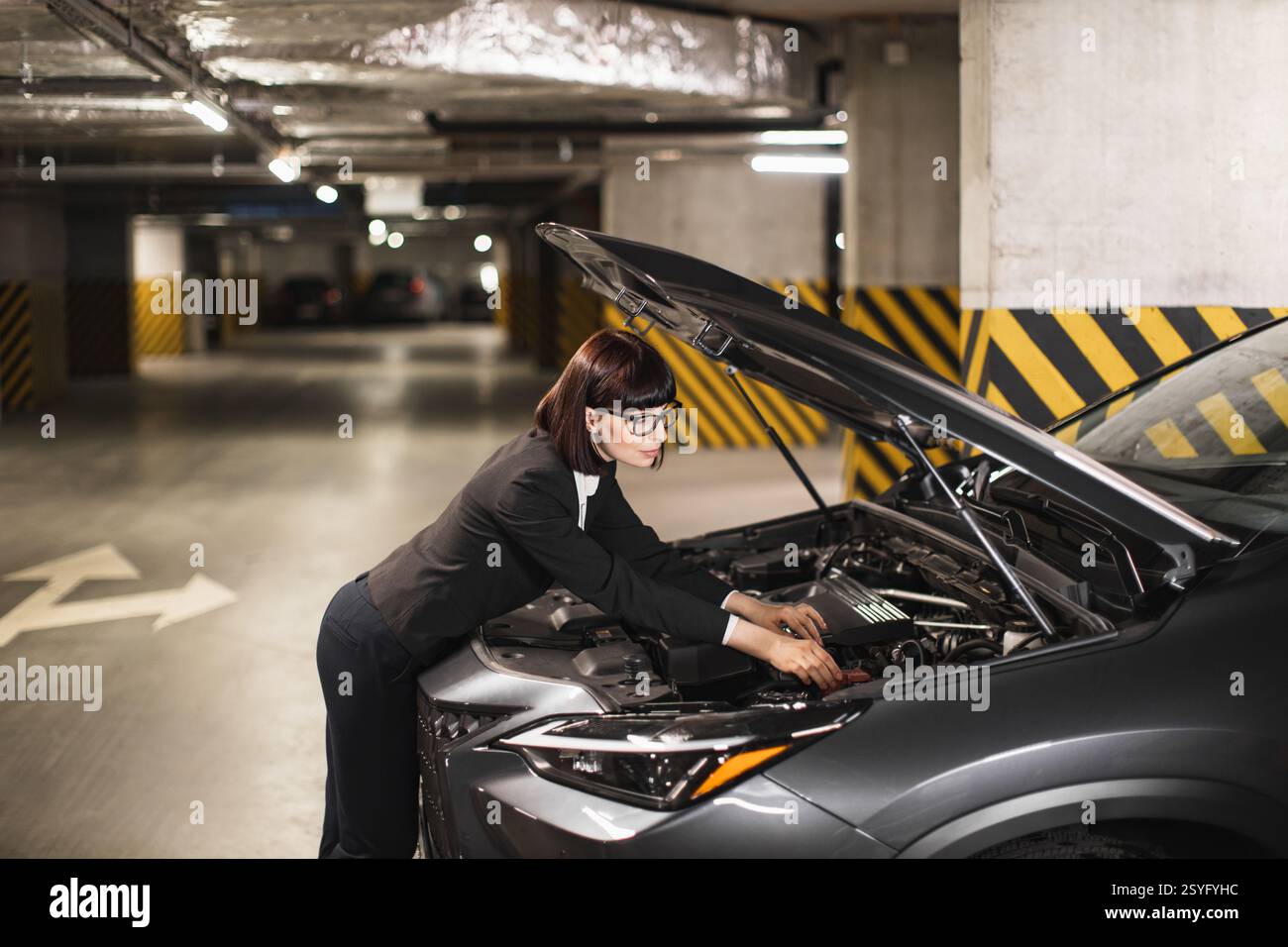 Caucasian adult businesswoman in professional attire repairs car engine under hood in ...