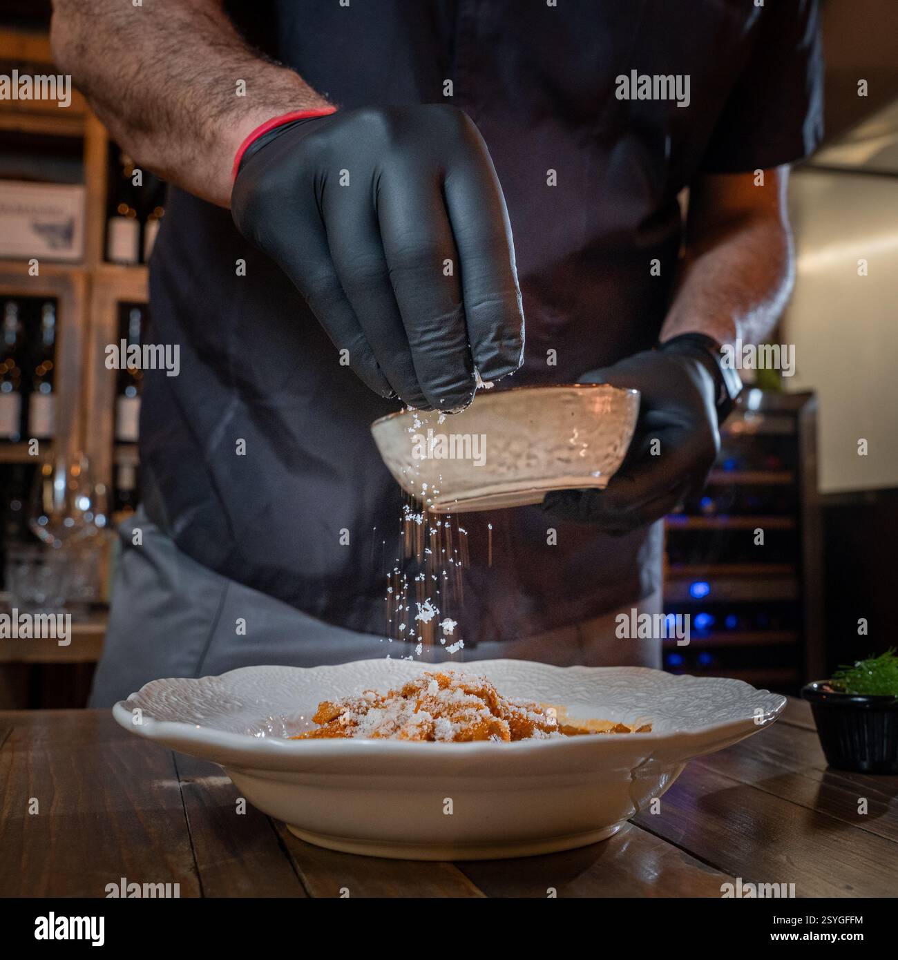 A professional chef wearing black gloves garnishing freshly made pasta ...