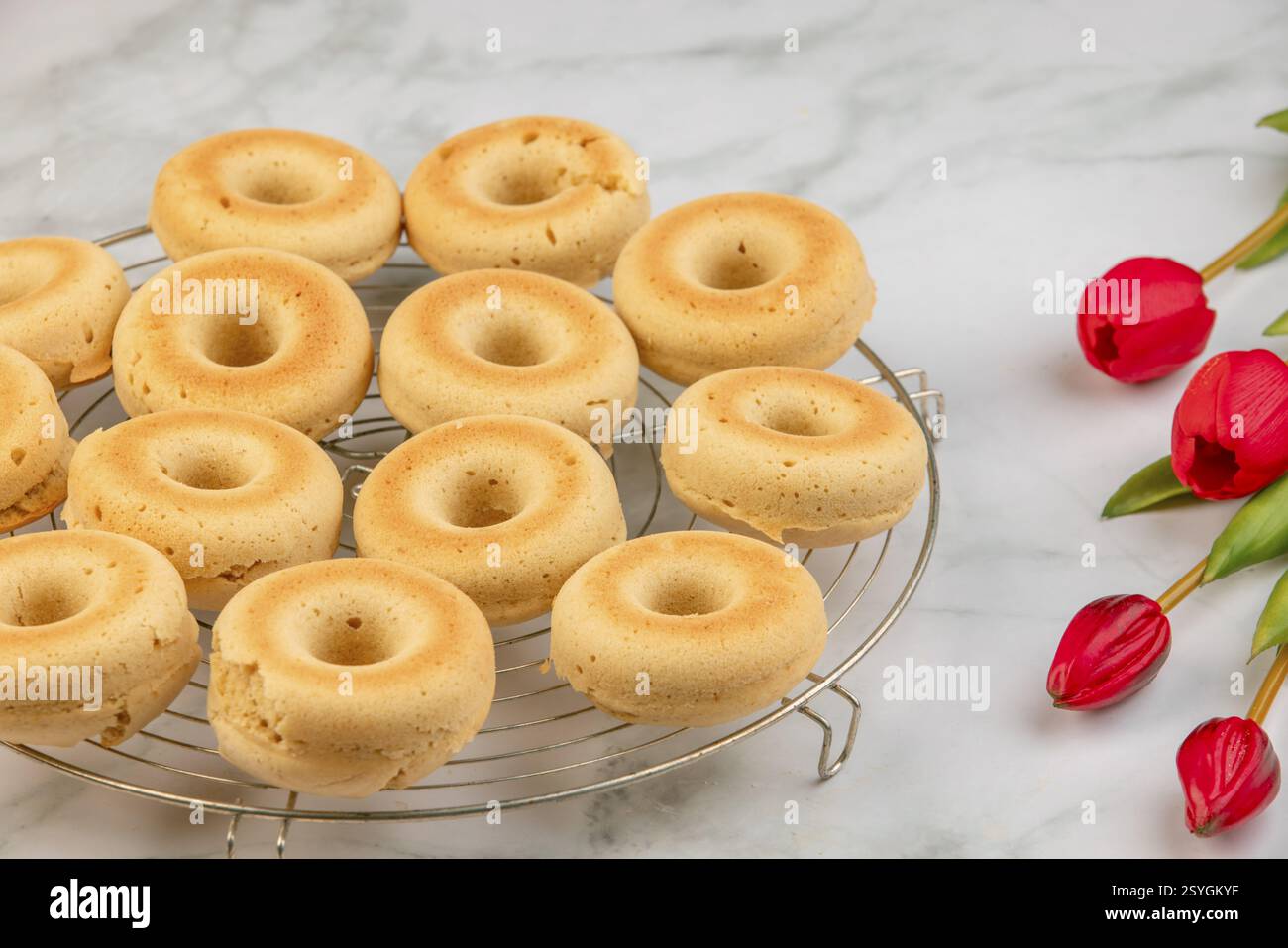 Fresh donuts on a cooling rack with red tulips on the side Stock Photo ...