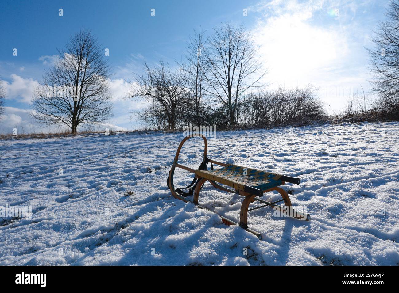 A wooden sled sits on a snow-covered slope under a clear blue sky with ...