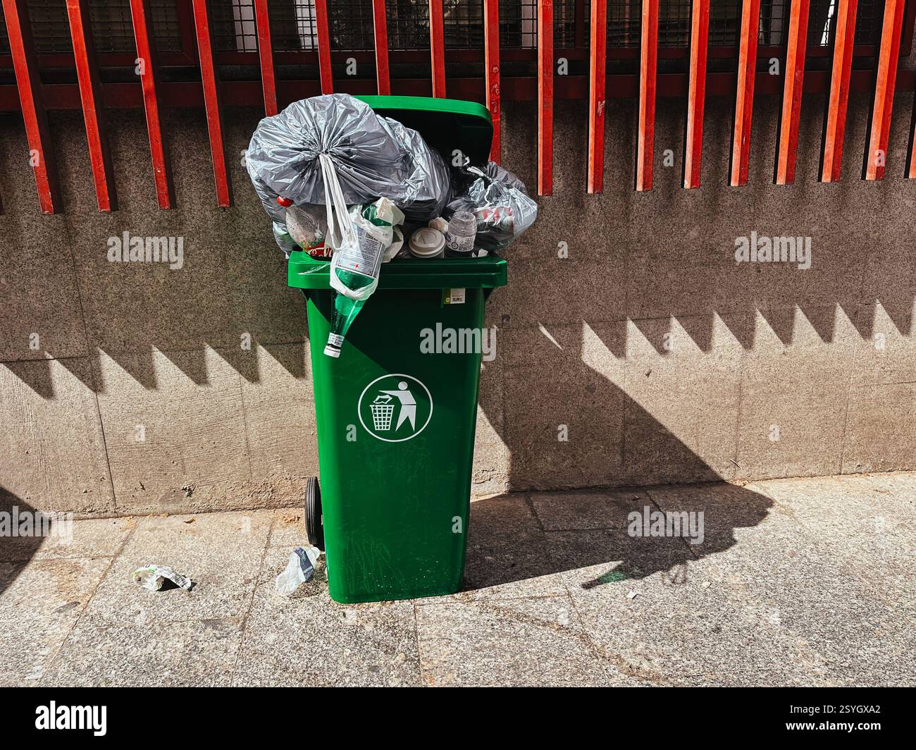 Green waste bin overfull with garbage on a city street. Plastic bags ...