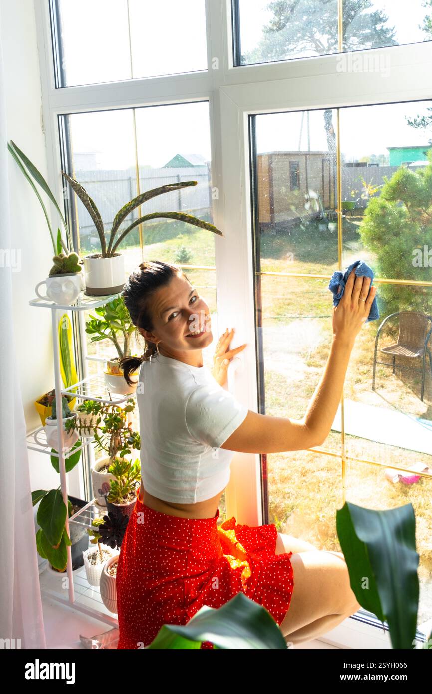 Woman manually washes the window of house with rag cleaner and mop inside the interior with home ...