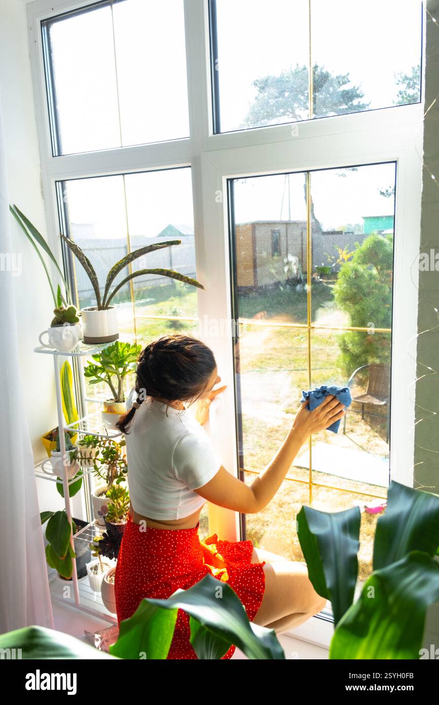 Woman manually washes the window of house with rag cleaner and mop inside the interior with home ...