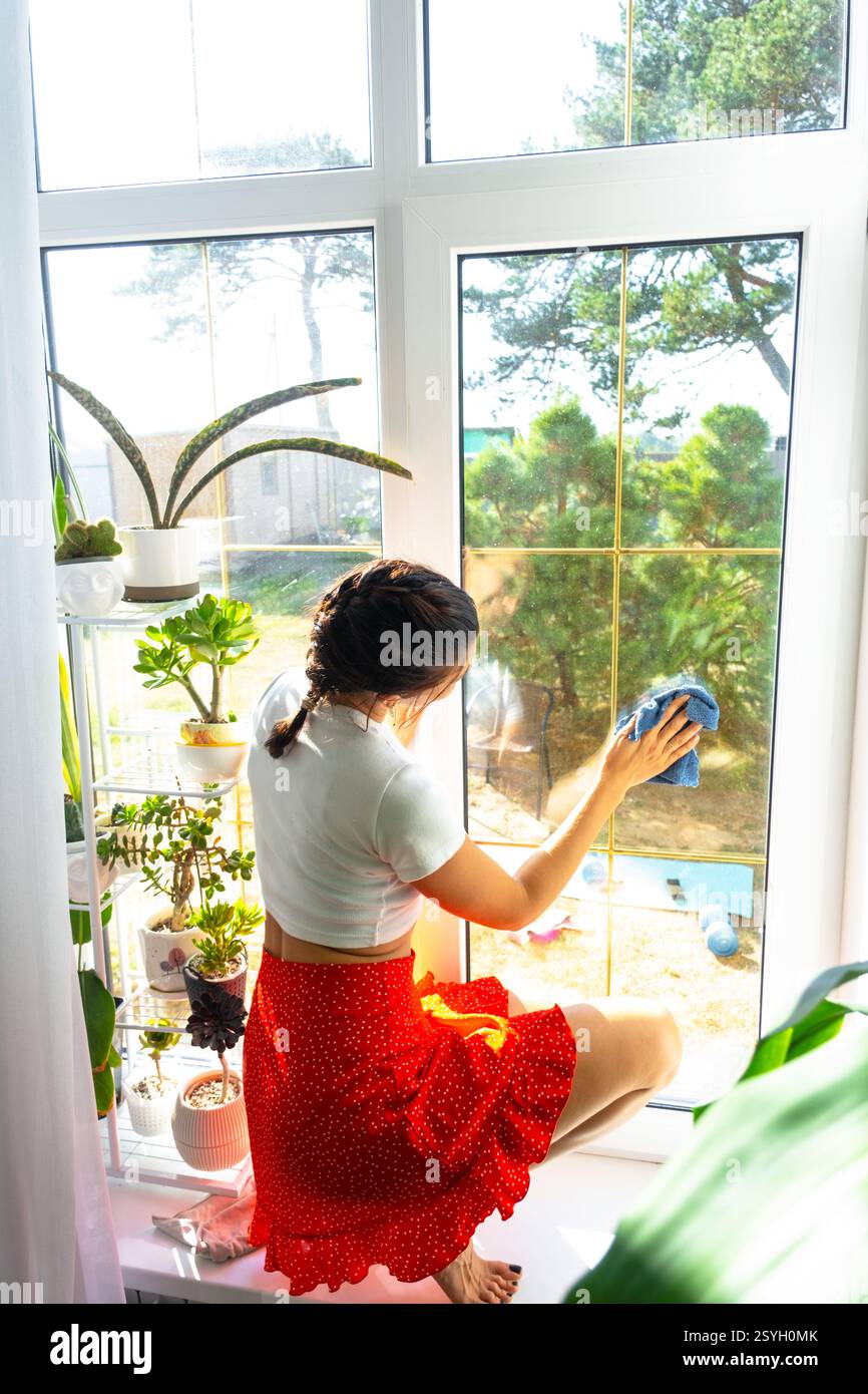 Woman manually washes the window of house with rag cleaner and mop inside the interior with home ...