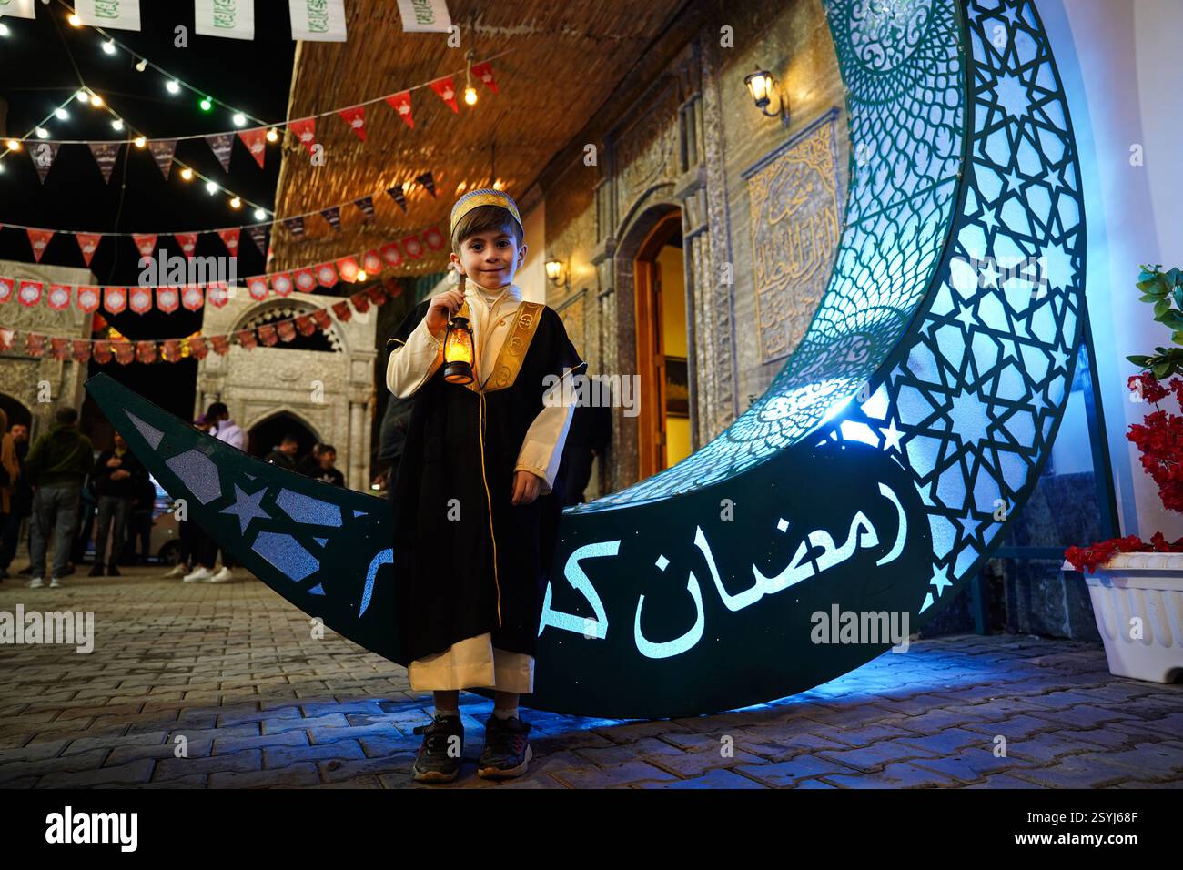 Mosul, Iraq. 28th Feb, 2025. A boy stands in front of Ramadan crescent ...