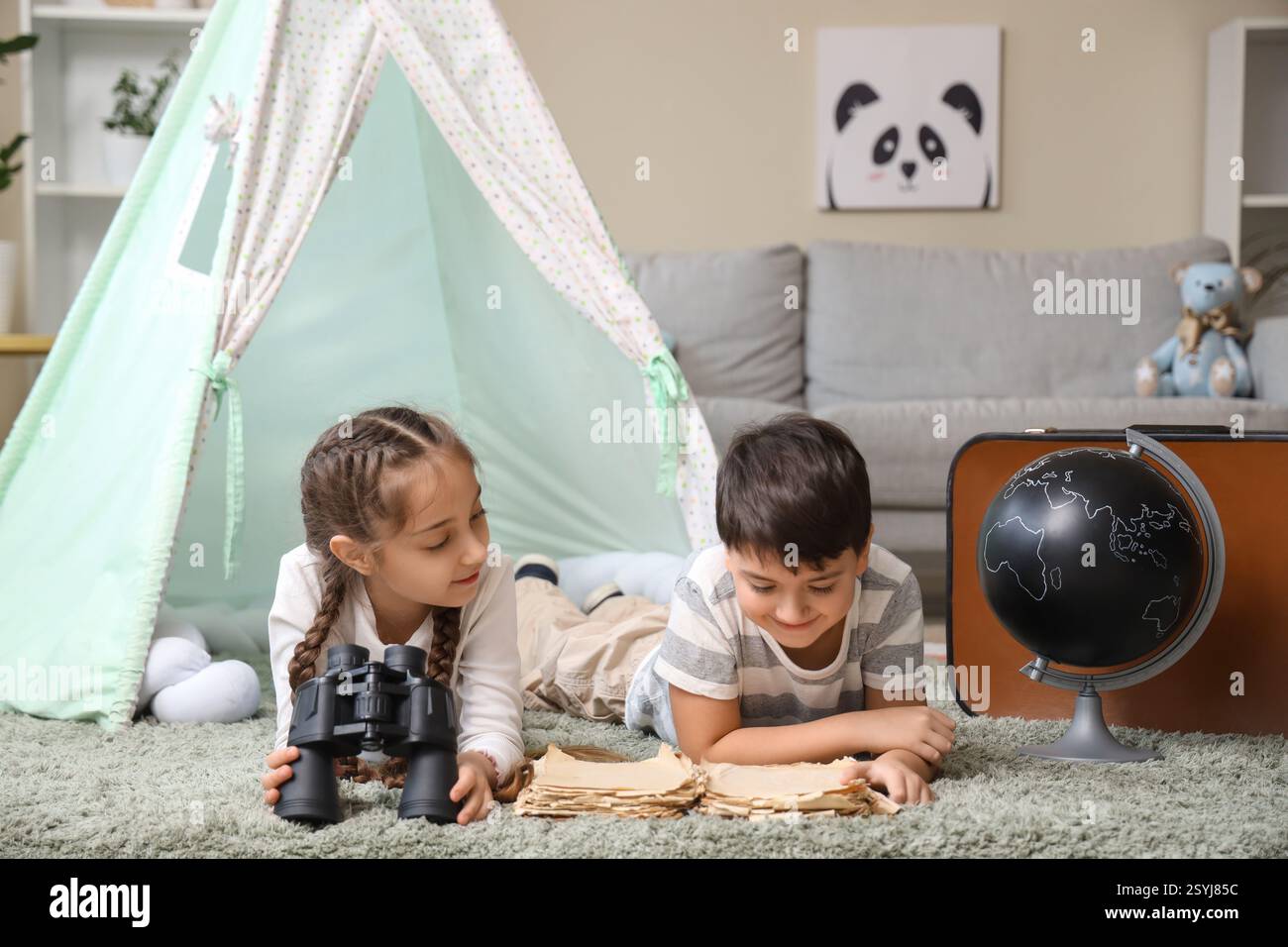 Cute children with binoculars reading adventure book on carpet at home ...