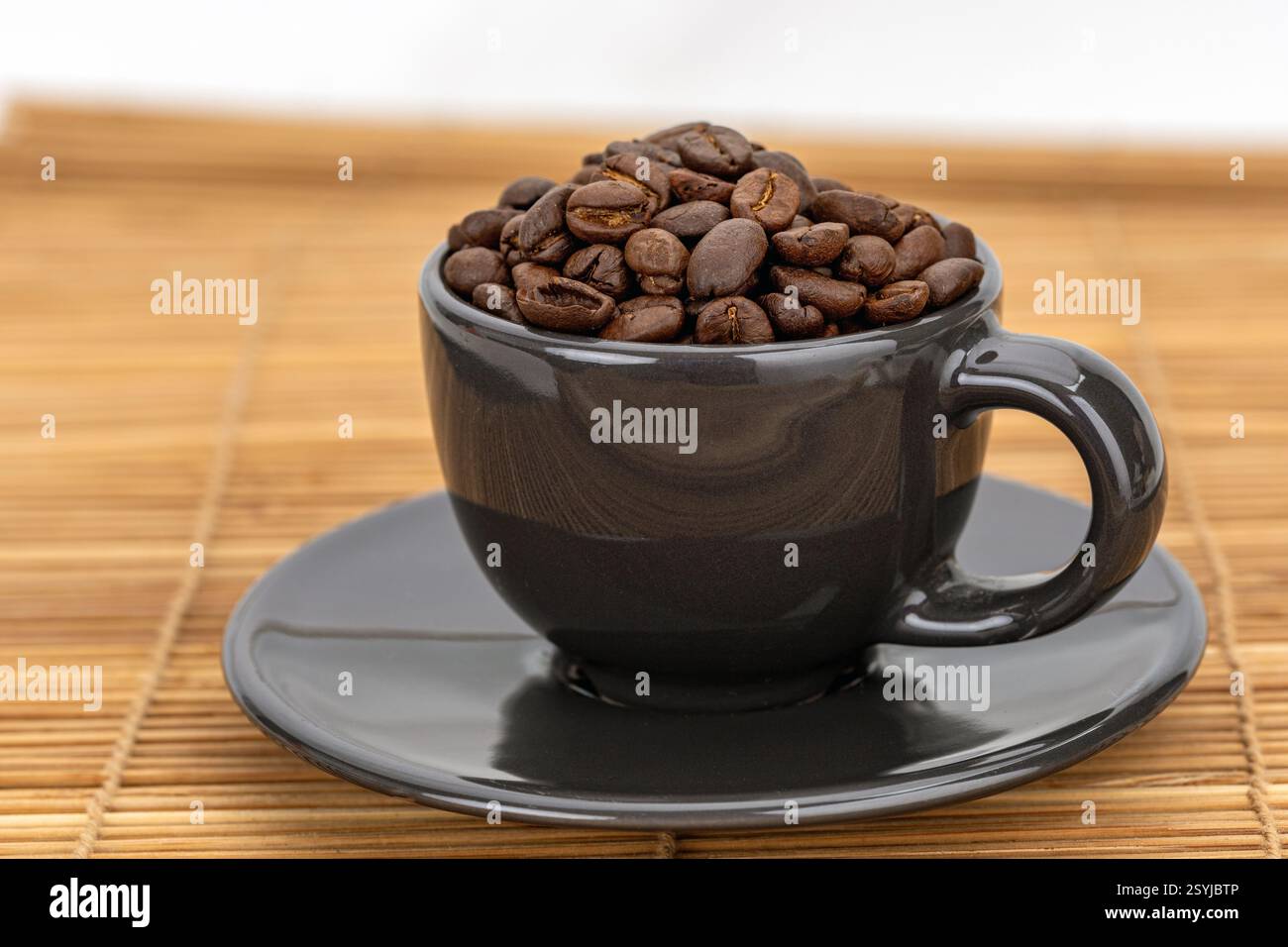 A black ceramic mug filled with roasted coffee beans gives off a rich ...