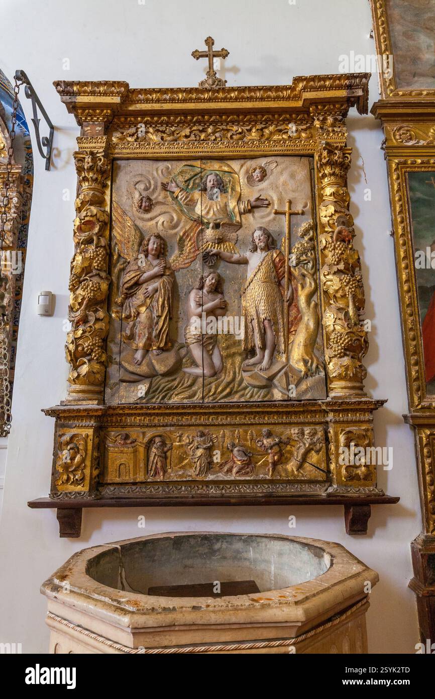 A religious altarpiece with a carved wooden relief depicting the Baptism of Christ, framed in ...