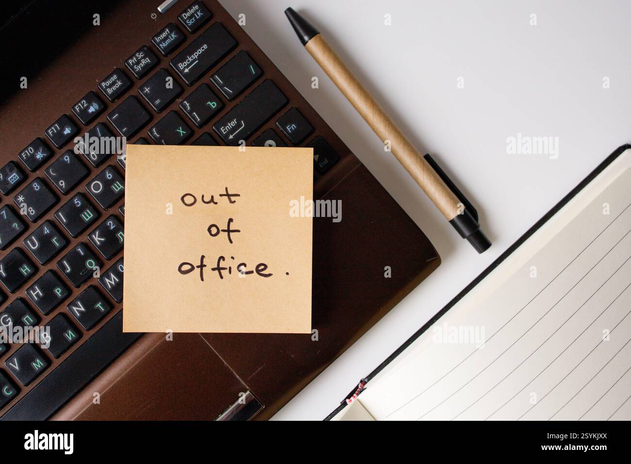 Sticky note with handwritten phrase out of office on a laptop with pen ...