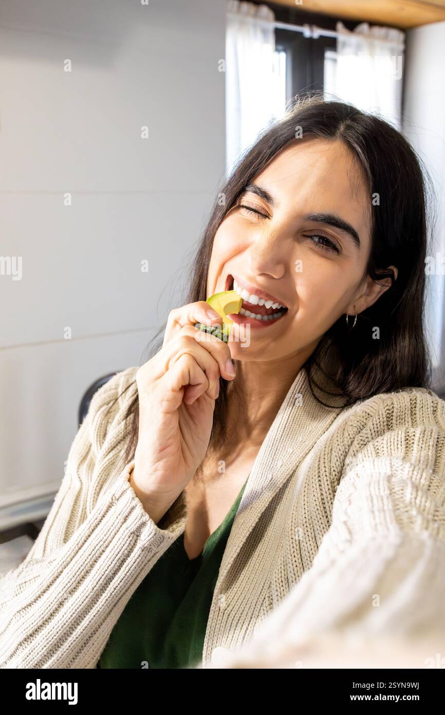 Happy woman playfully winking while taking a bite of fresh avocado in a ...