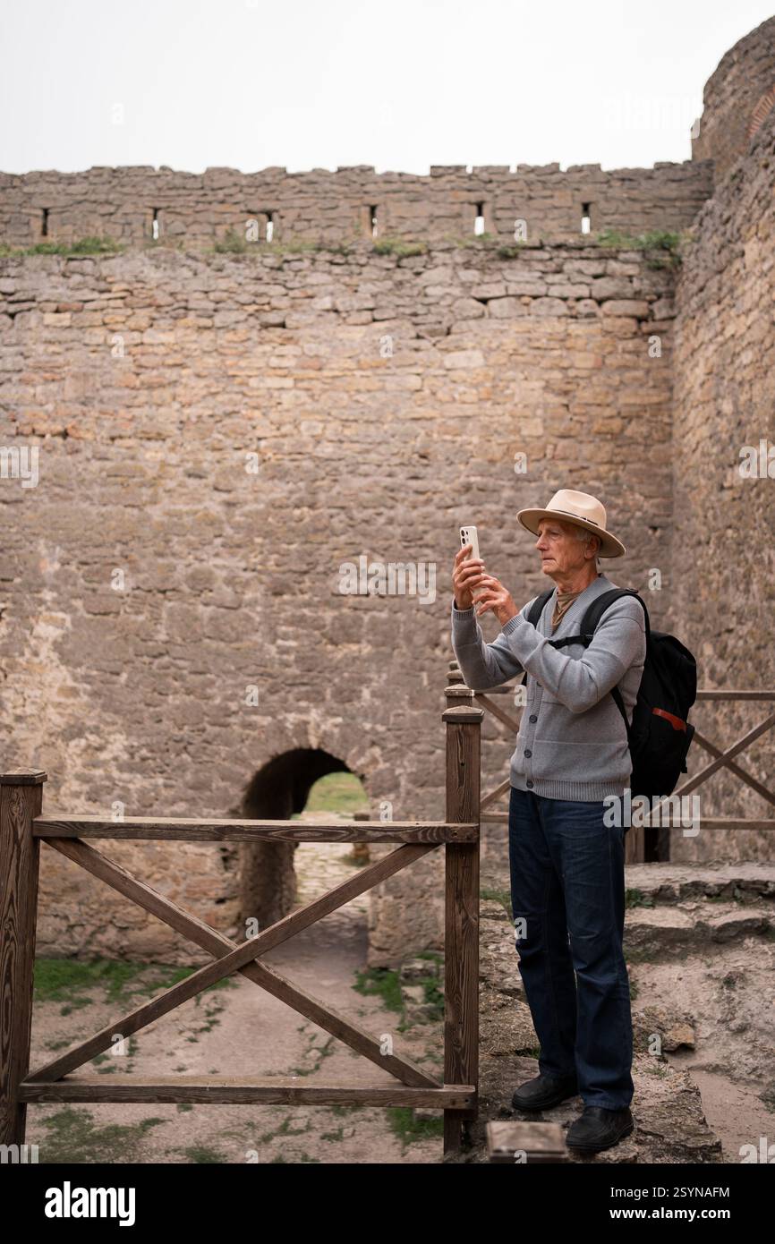 Elderly man in hat visiting medieval fortress taking photo for memory ...