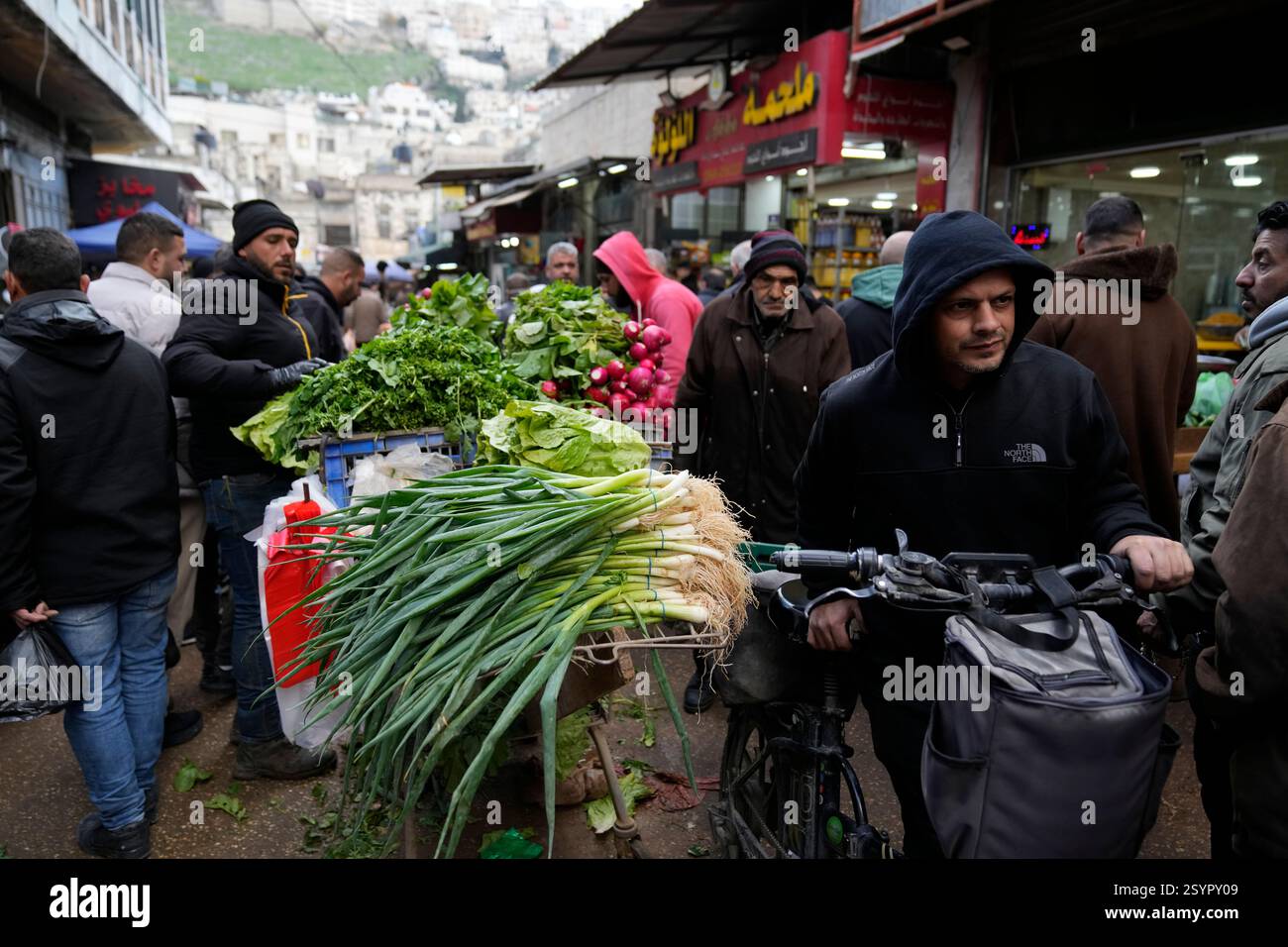 A Palestinian vendor displays fresh vegetables while residents shop for ...