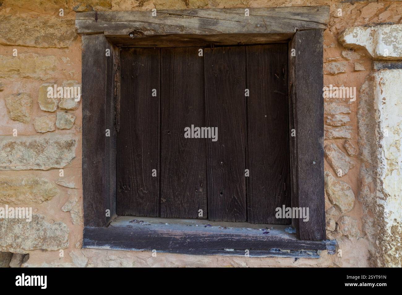 A dark, weathered wooden shutter covers a window opening in a rough ...