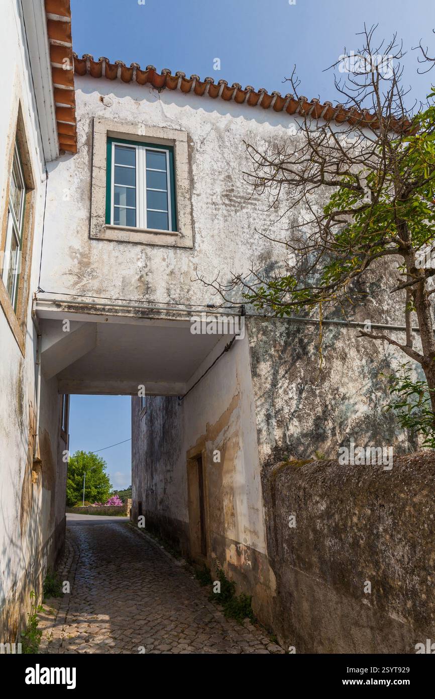 A narrow cobblestone street passes through an arched passage between ...
