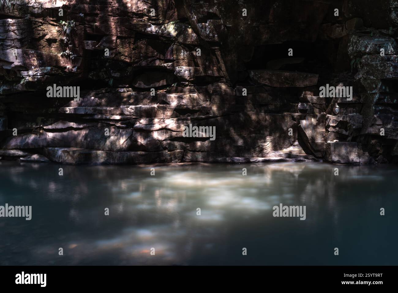 A shaded pool lies quietly at the base of a steep rocky wall Stock ...