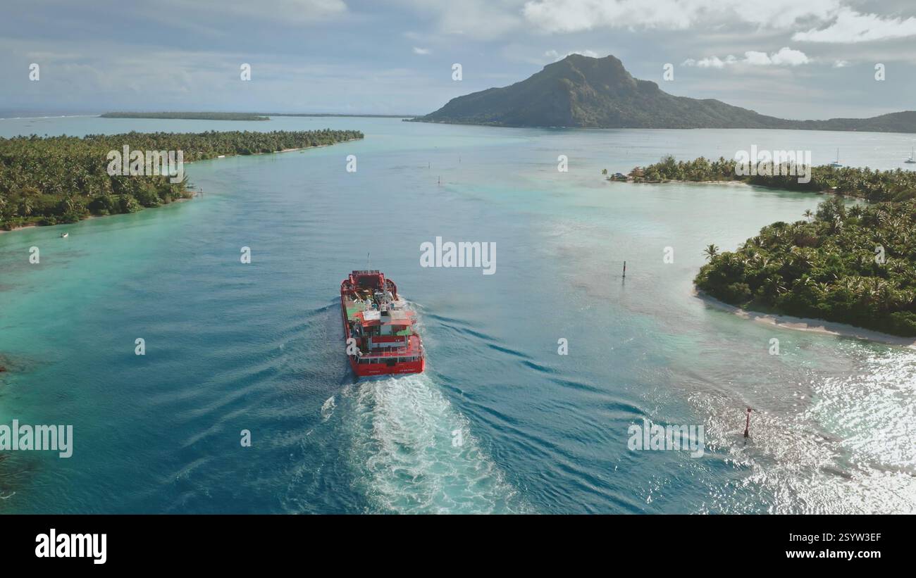 Aerial drone of red cargo ship sailing through crystal clear waters of ...