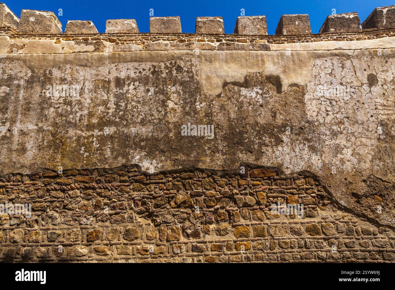 weathered stone wall with a crenellated top, revealing layers of ...