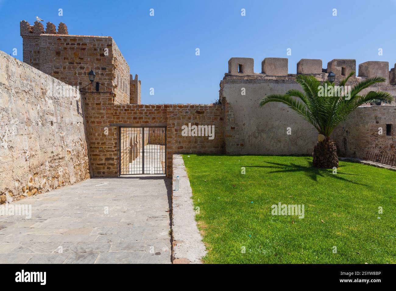 historic courtyard with a stone wall, a crenellated tower, a lush green ...