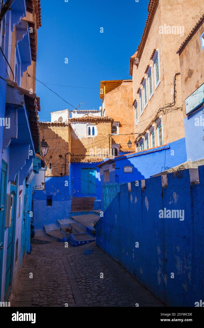 narrow, winding street in a blue-washed town, featuring buildings with ...
