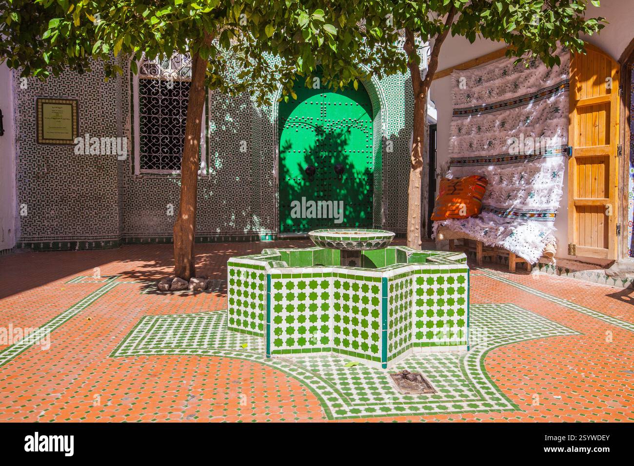 A serene courtyard featuring a tiled fountain, lush green trees, and a ...