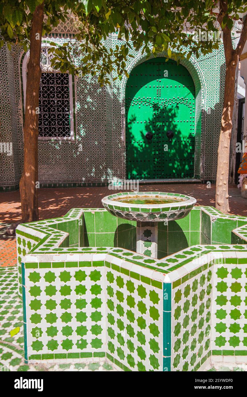 A serene courtyard featuring a tiled fountain, lush green trees, and a ...