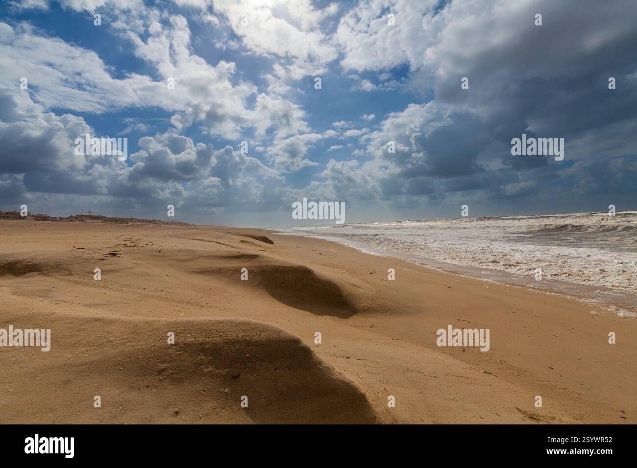 A vast sandy beach stretches towards a turbulent ocean under a dramatic ...