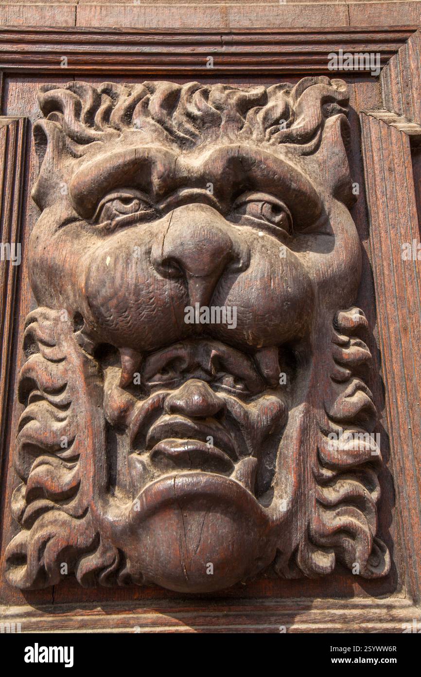 Close-up shot of a weathered, carved wooden panel featuring a grotesque ...