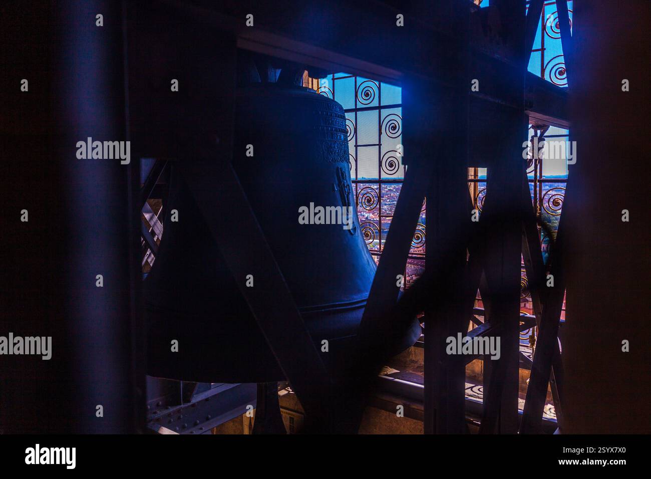 A large, dark bell hangs silhouetted against a backdrop of colorful ...