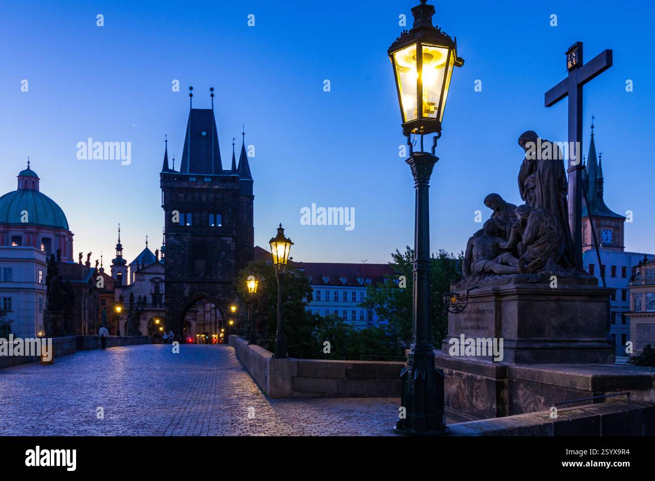 A cobblestone bridge at twilight, featuring a statue with a cross and ...