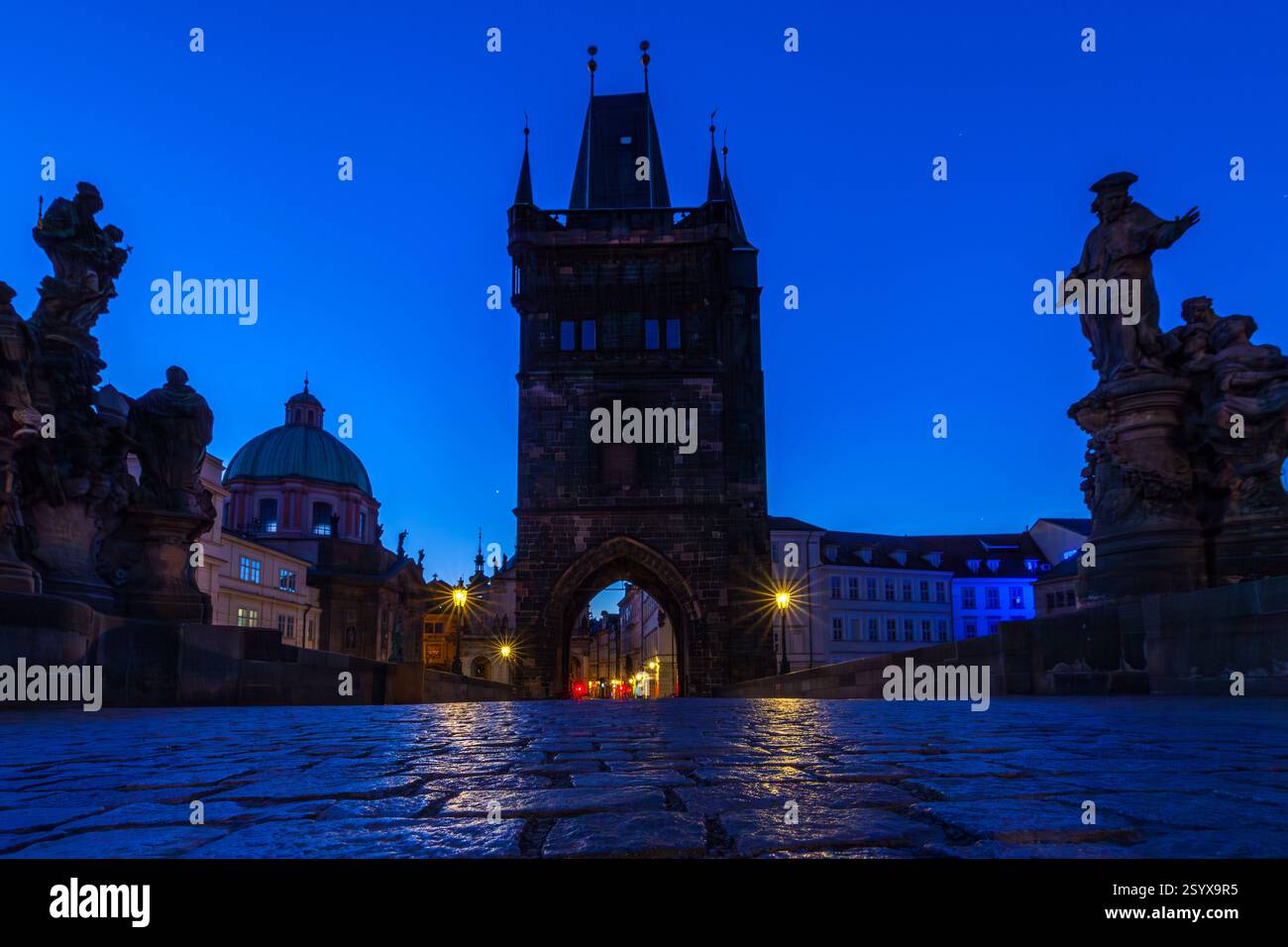 A cobblestone bridge at night leading towards a tall, silhouetted tower ...