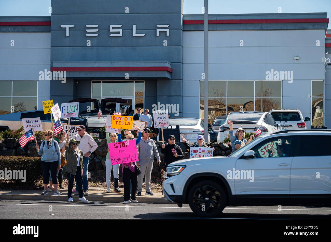 A car drives by a Tesla protest at a Tesla Dealership with protesters ...