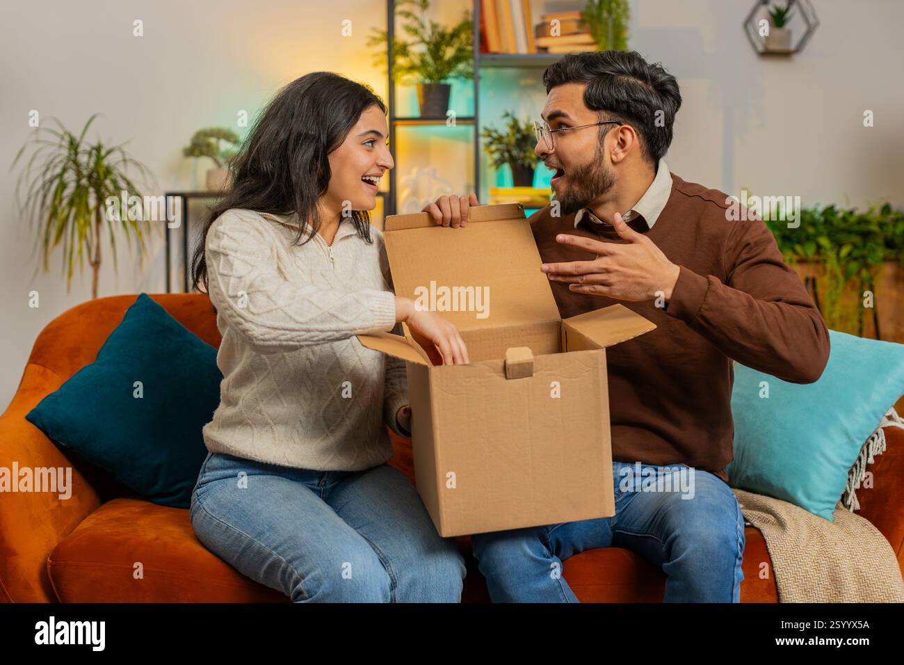 Happy excited couple open cardboard box together sitting on sofa at ...