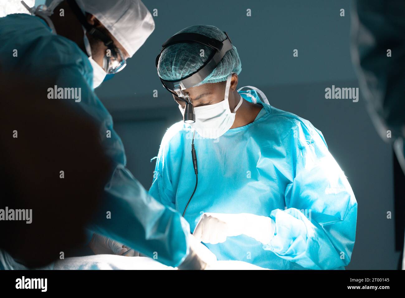Diverse surgeons wearing surgical gowns operating on patient in ...