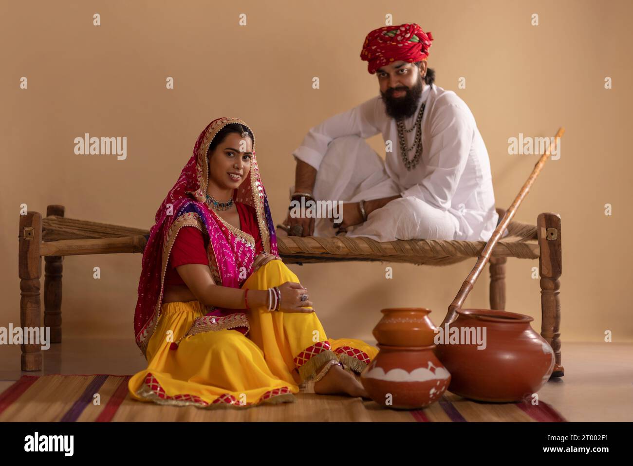 Rajasthani man sitting on cot while his wife sitting on mat at home ...