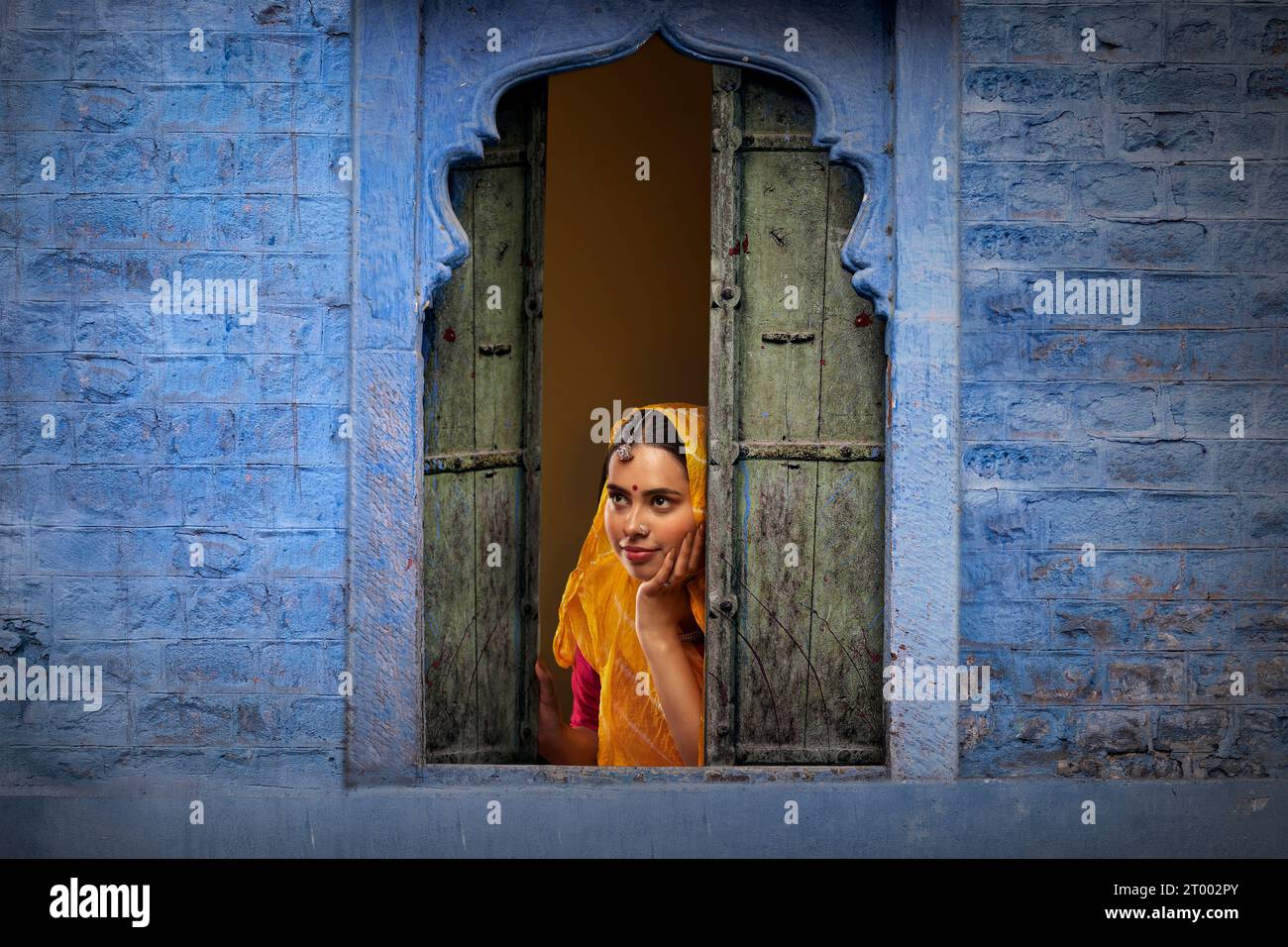 Rajasthani young woman peeking out through window with hand on cheek ...
