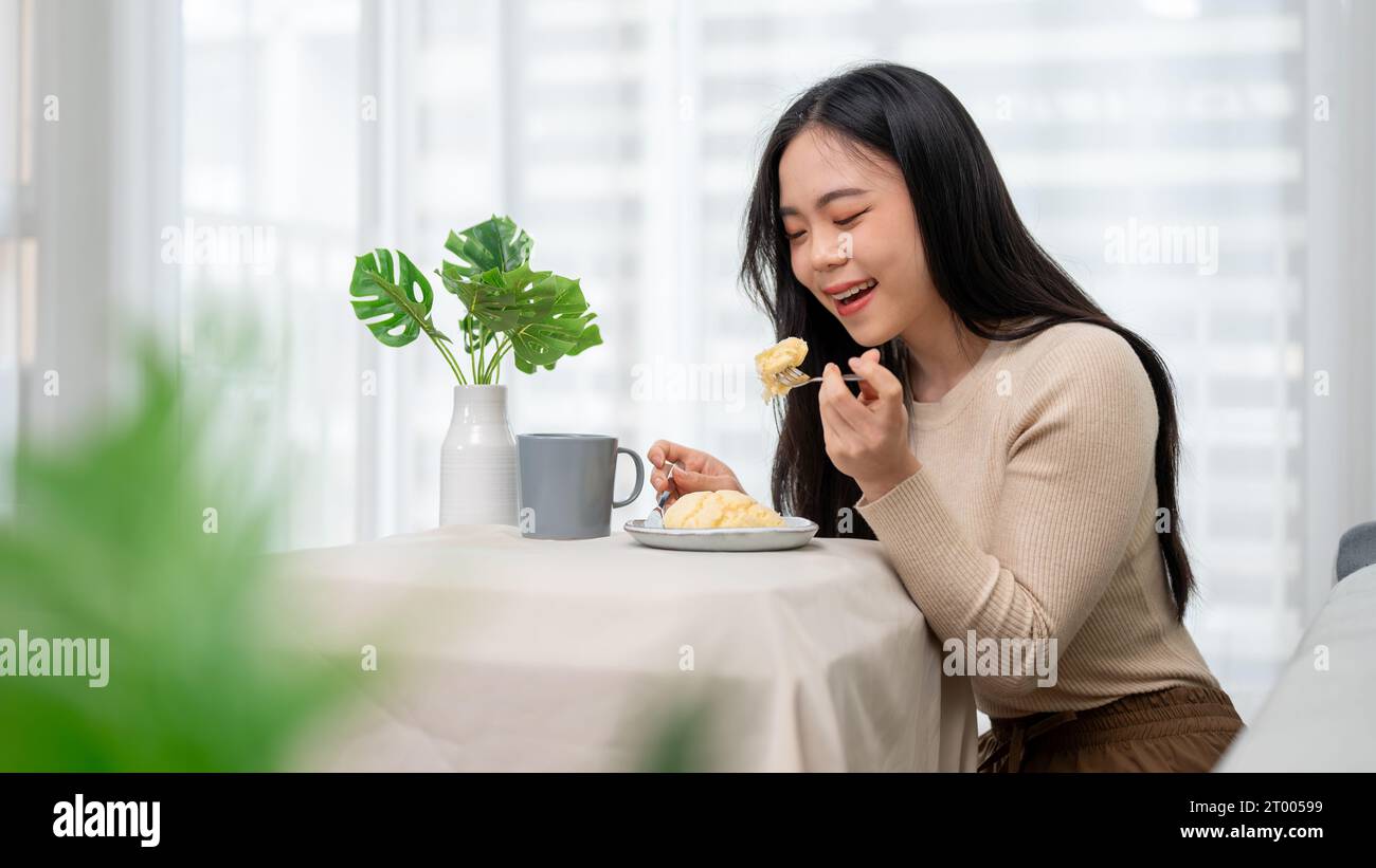 A beautiful and cheerful young Asian woman enjoying her breakfast at a ...