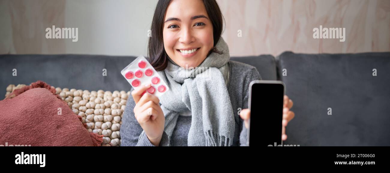 Smiling korean girl shows smartphone screen, medication in hands ...