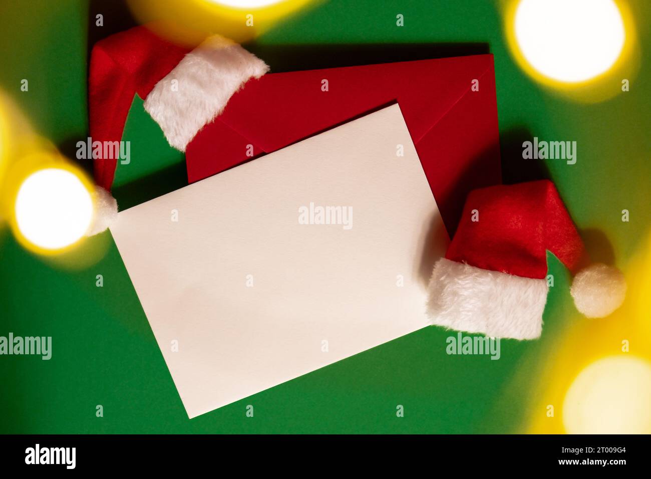 Santa hat with empty paper card note envelope on green background. Copy ...