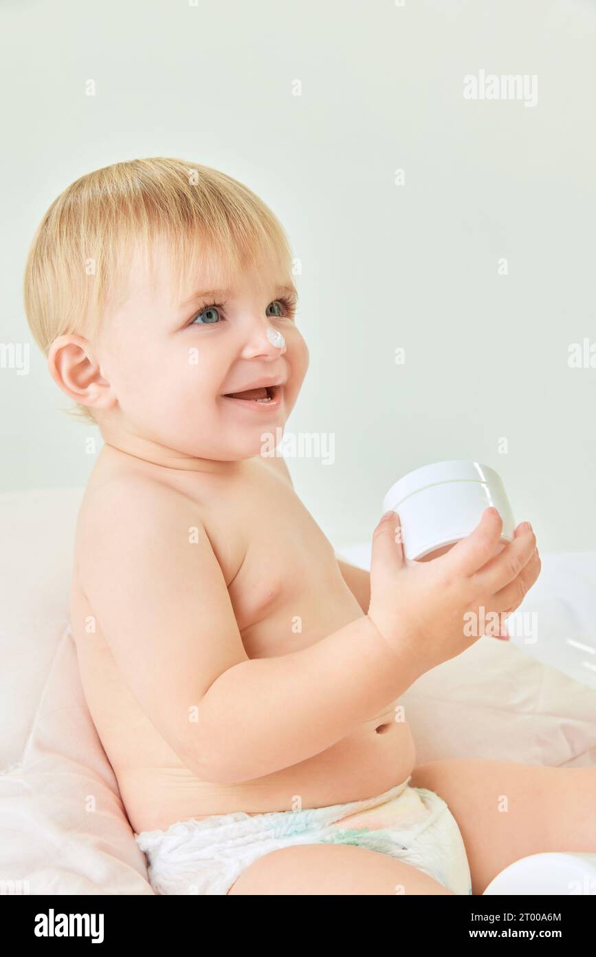 Cream on nose. Cute, beautiful child, little baby girl in diaper in bed ...