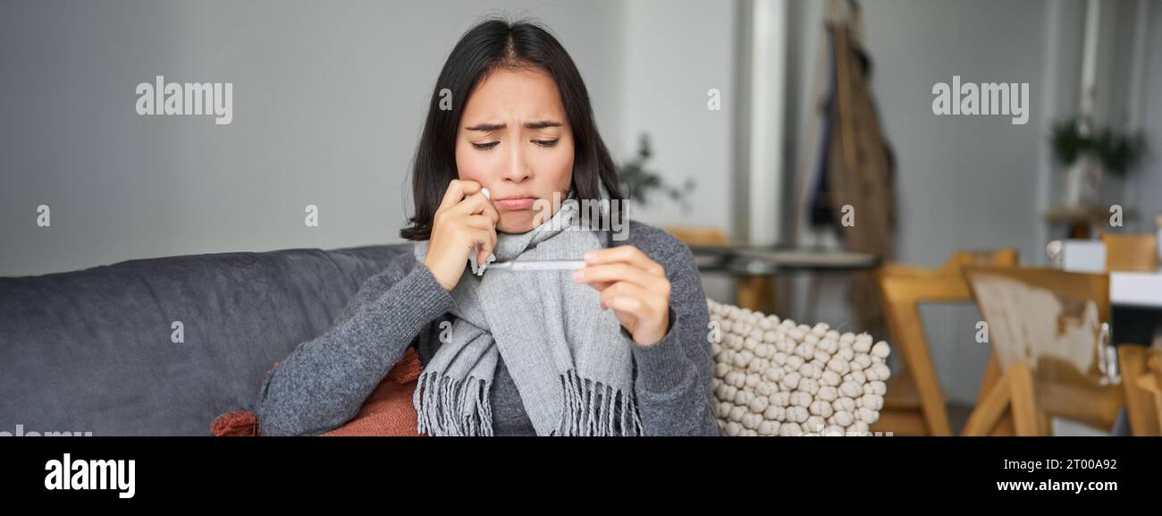 Girl looks upset at thermometer with high temperature, has fever ...