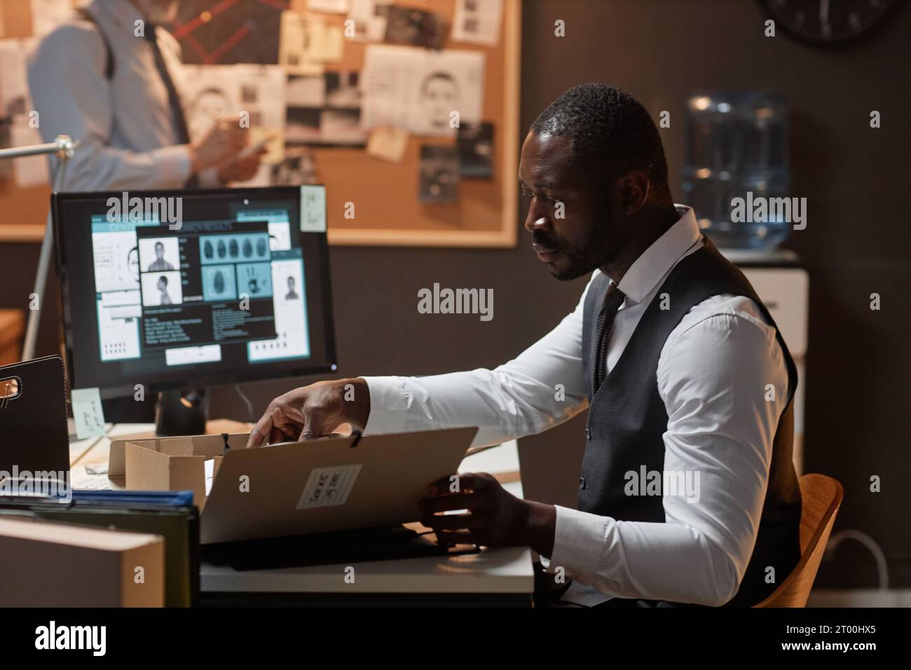 Side view portrait of Black man as detective reading case files at desk ...