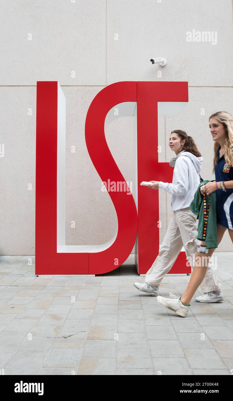 Undergraduate students walking in front of the red lettering signage denoting the London School ...