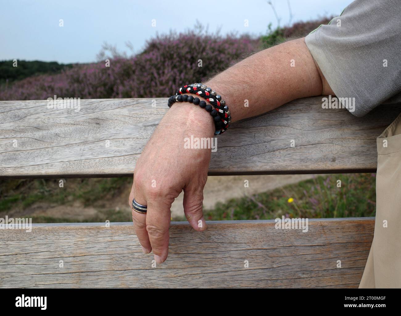 A man's arm lying across the back of a wooden bench. He wears beaded ...