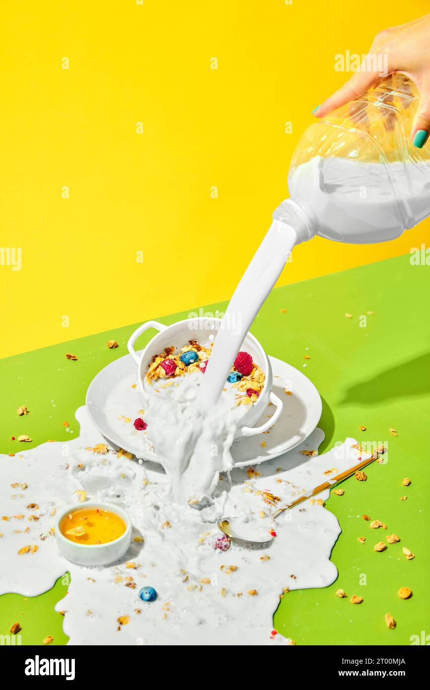 Too many milk. Female hand pouring milk into bowl with muesli, cereal with berries against green ...