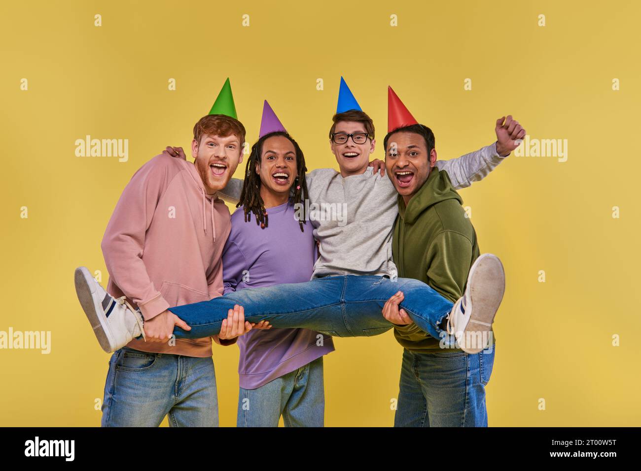 four cheerful men in birthday hats smiling at camera and holding one of ...