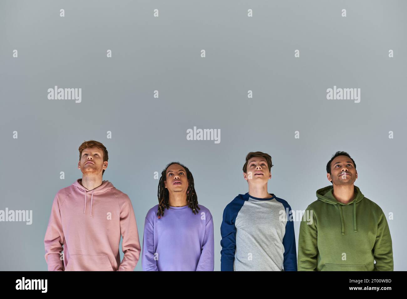 four smiling young men in casual bright attire looking up on grey ...