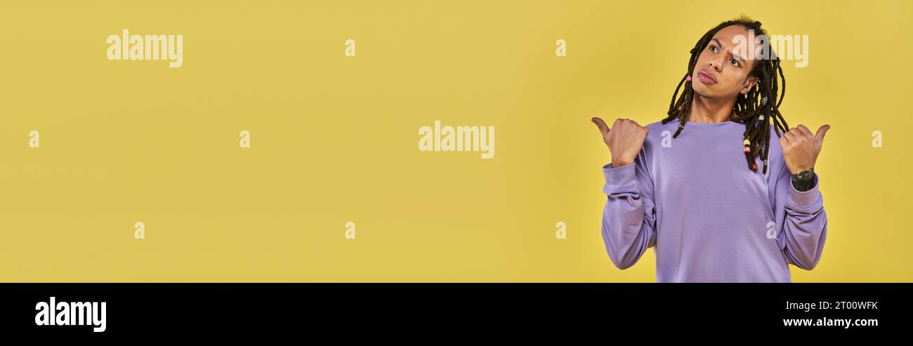 puzzled young man with dreadlocks thumbs pointing different ways on ...