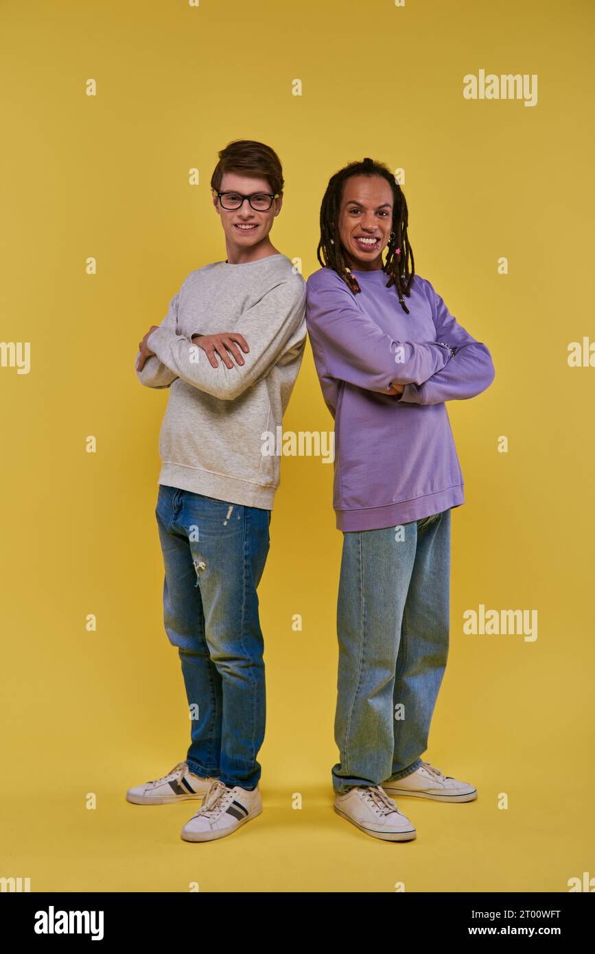 two cheerful multicultural friends standing back to back and smiling at ...