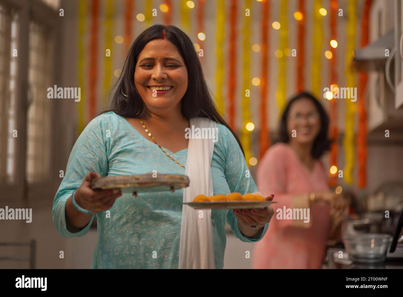 Sister in laws in the kitchen,preparing to serve sweets during the festival of Diwali Stock ...